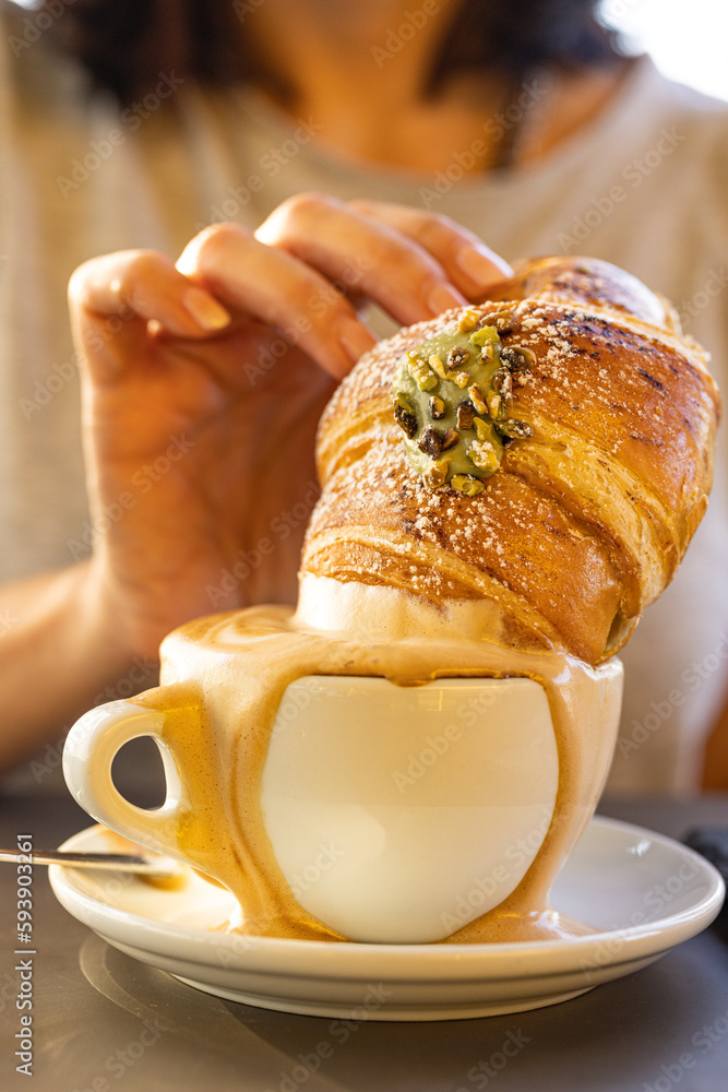 Cliente di un bar a colazione mentre immerge un cornetto al pistacchio ...
