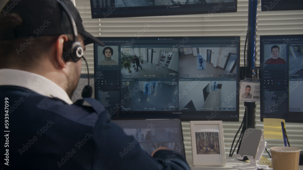 Security officer in headset monitors CCTV cameras on computer in ...