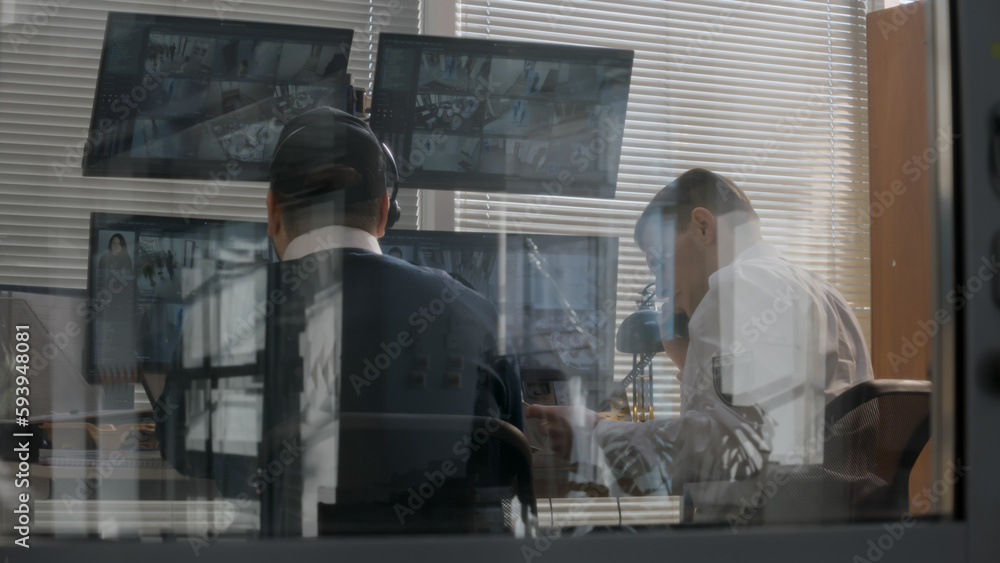 Security officers monitor CCTV cameras on computer and use landline ...