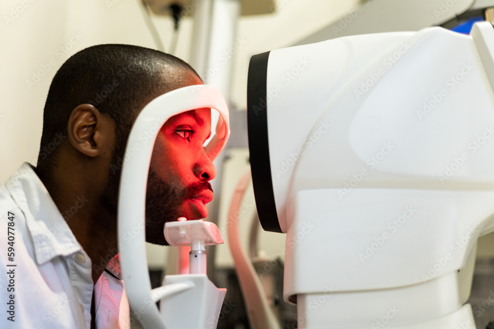 A dark-skinned man is undergoing a vision test using a corneal ...