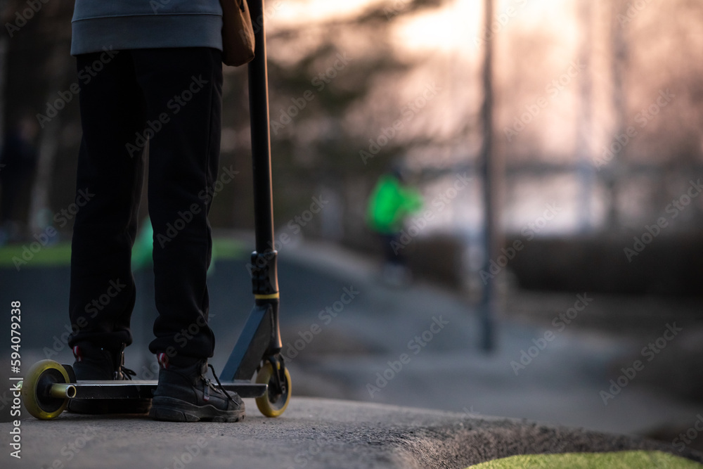 Closeup, the boy's legs with a stunt scooter in a skate park make jumps ...