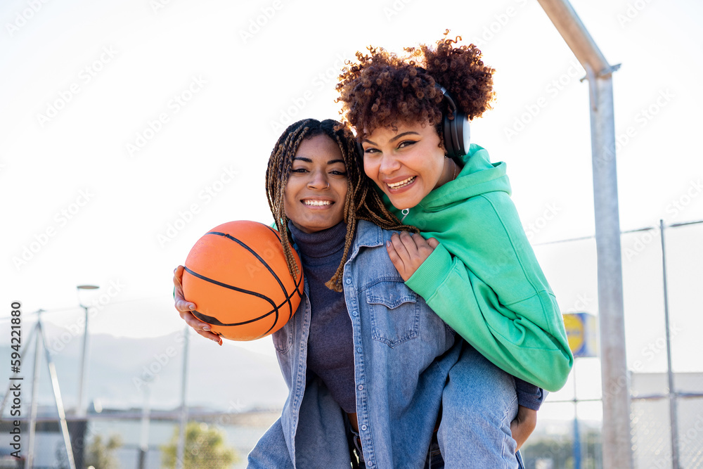 Two young, dark-skinned girls have fun on a basketball court. The girl ...