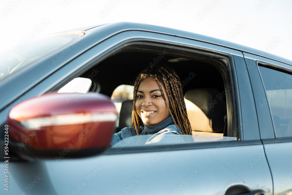 Dark-skinned young woman with braids sitting in a car looking at the ...