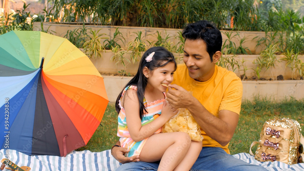 Modern Indian father offering wafers / chips to his little girl ...