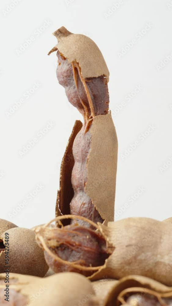 The tamarind fruit is half peeled, rotates on a white background on a ...