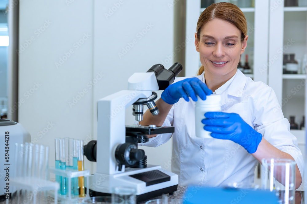Female scientist in lab coat and gloves using microscope microbiologist ...