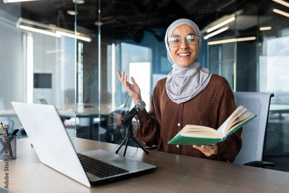 Online teaching. Young Muslim woman in hijab teacher sits at desk in office in front of laptop ...