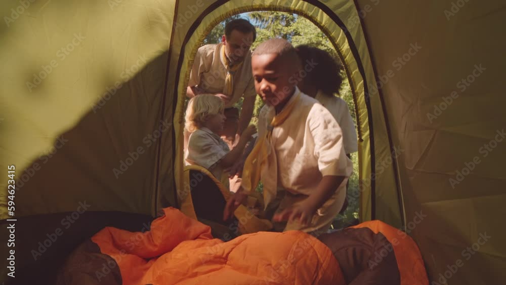 Little African American boy scout putting sleeping bag in tent while ...
