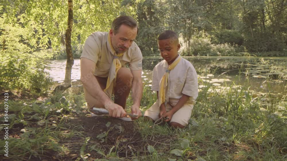 Mid adult Caucasian male scout leader teaching little African American ...