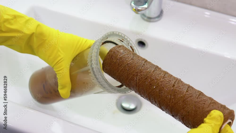 Plumber working in yellow protective gloves holds a dirty water filter ...