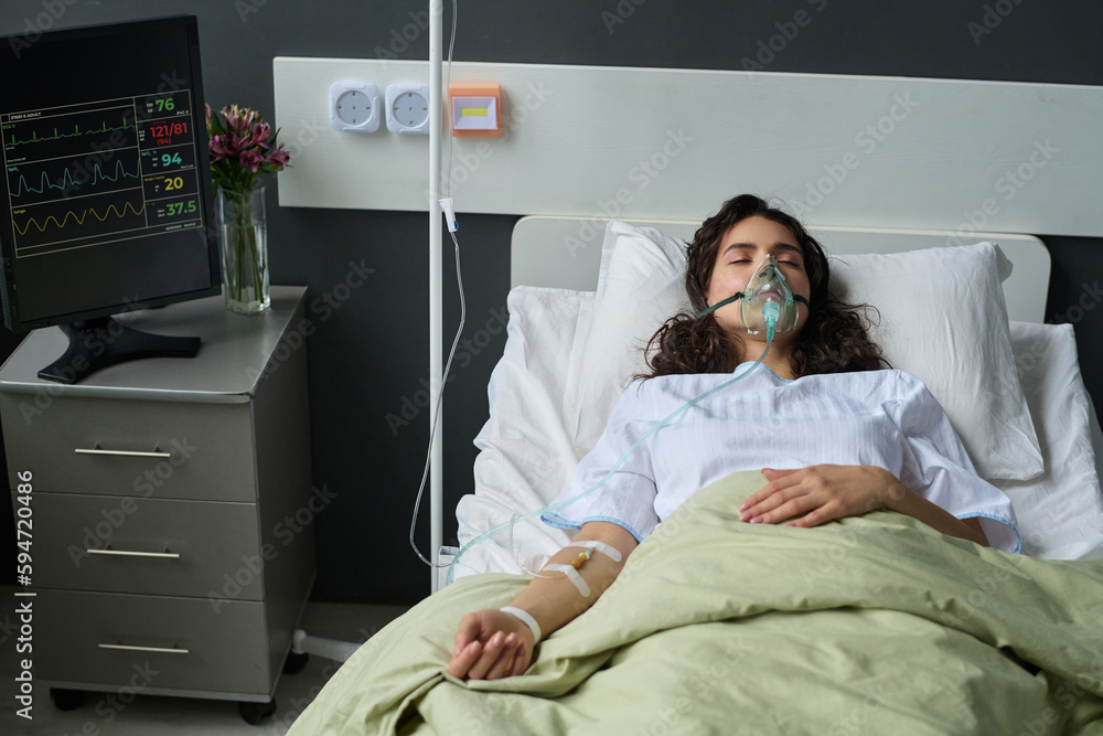 Unconscious young woman lying on bed with oxygen mask during treatment ...