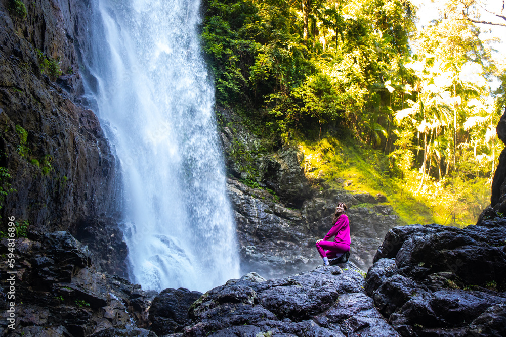 hiker girl sitting on rocks in front of large tropical waterfall in ...