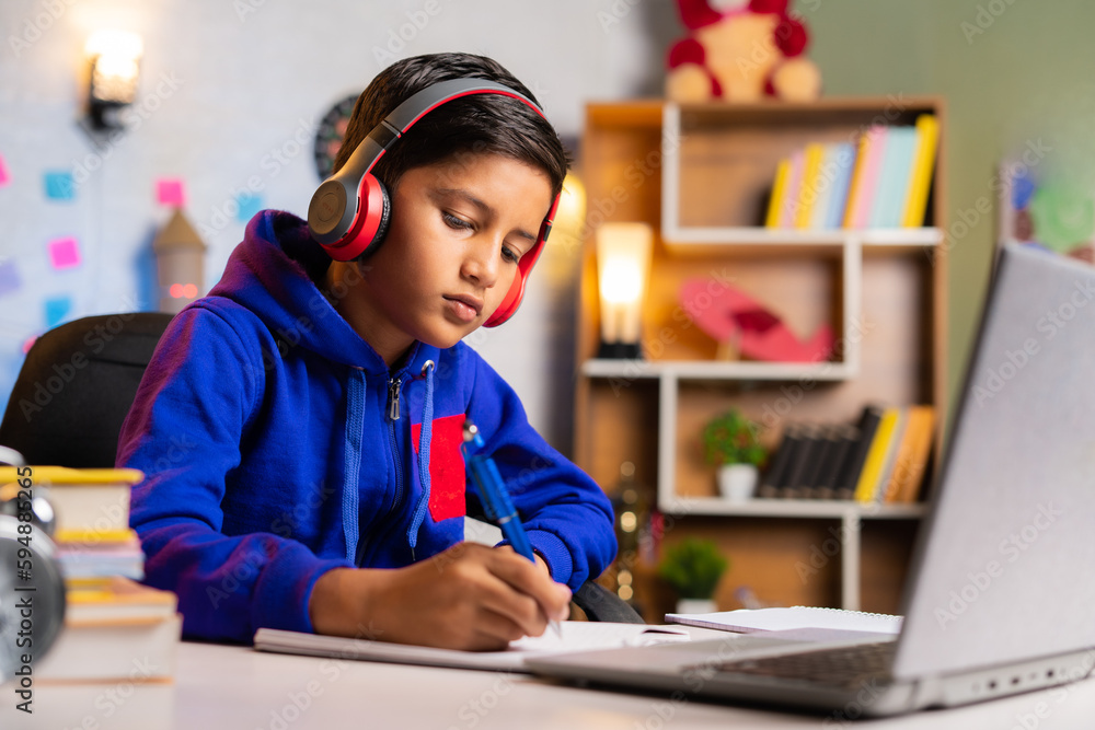 Indian kid making notes from online class on green screen laptop at ...