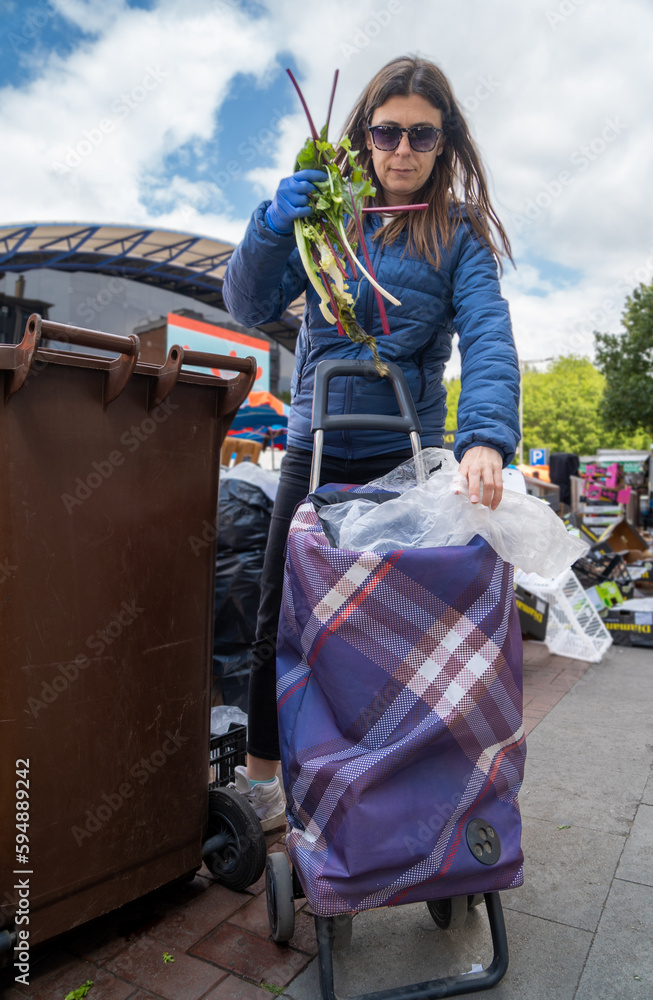 Young homeless woman holding lettuce and vegetables from the trash in ...