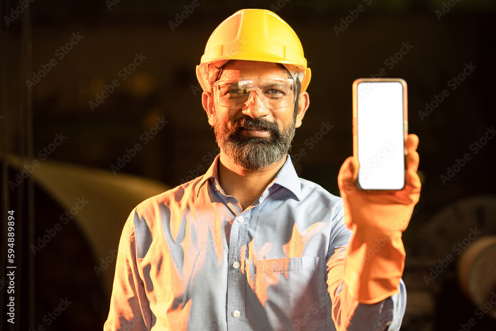 Indian male engineer wearing yellow helmet showing smart phone with ...