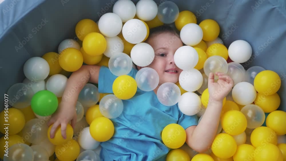 a child play in a dry pool with colored balls. happy family kid dream ...