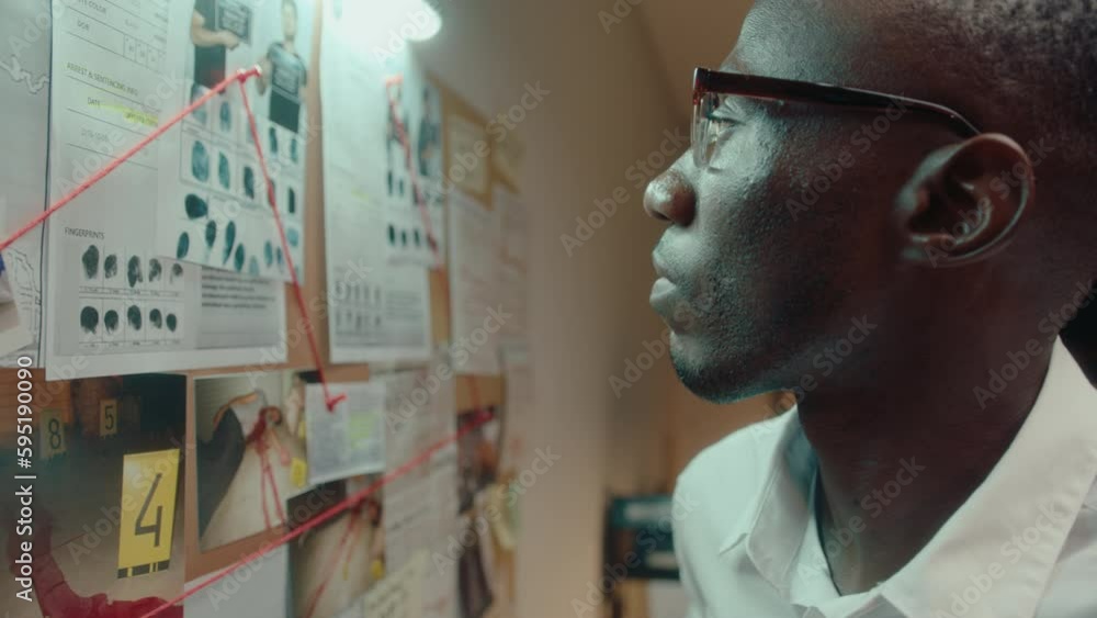 Thoughtful black detective standing in his office at night, looking at ...