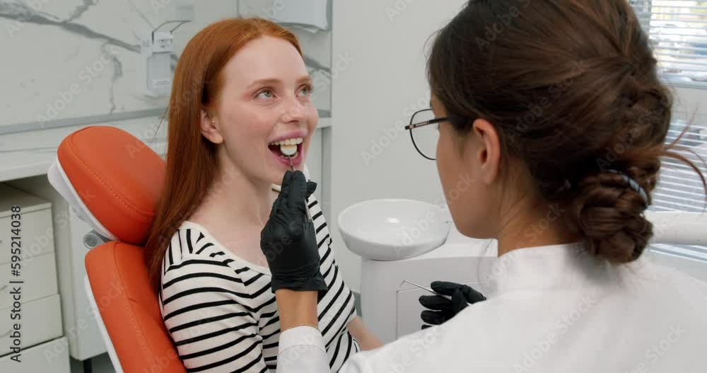talented female doctor probing red-haired woman's teeth with dental ...
