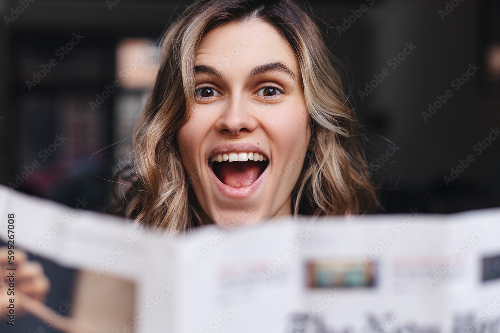 Surprised casual woman reading newspaper and open mouth, laughing while ...