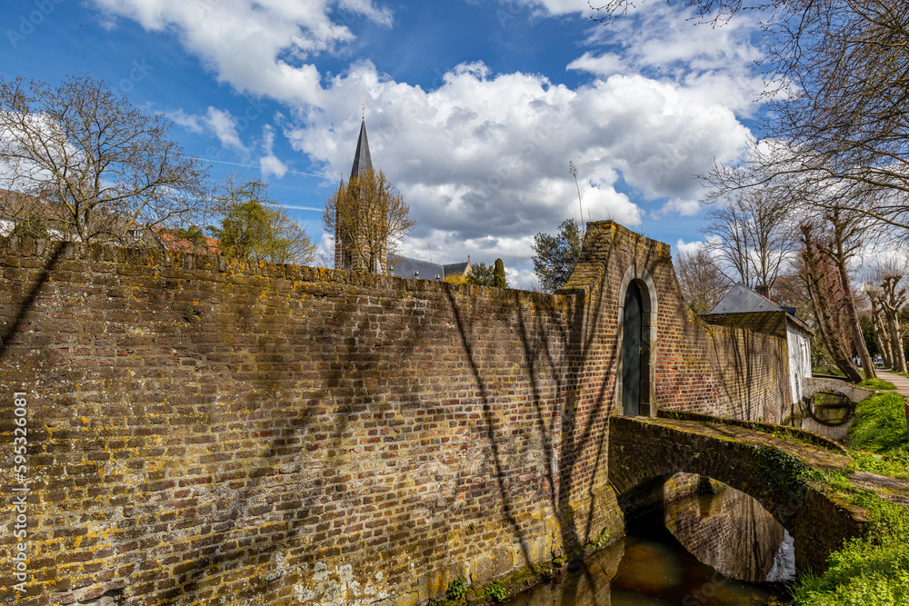 Old brick wall with a gate and small bridge along canal, bell tower of ...