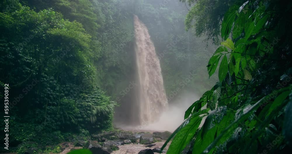 Epic Nungnung waterfall flows from a high cliff in tropical green ...
