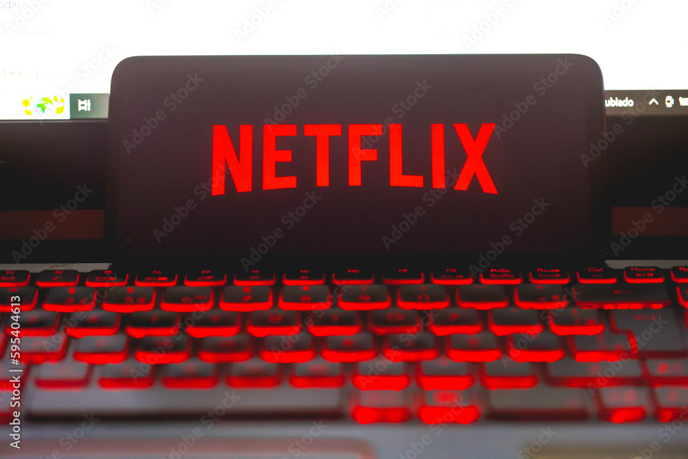 The Netflix logo on a cell phone screen resting on top of a lighted ...
