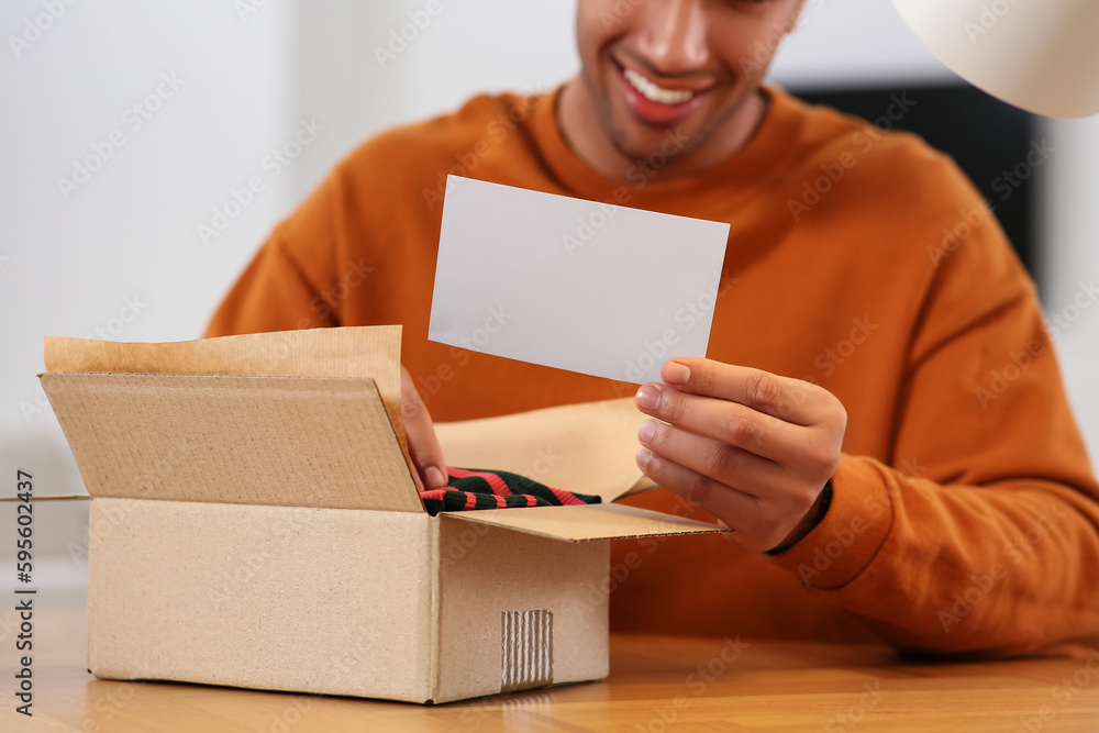 Young man holding greeting card near parcel with Christmas gift ...