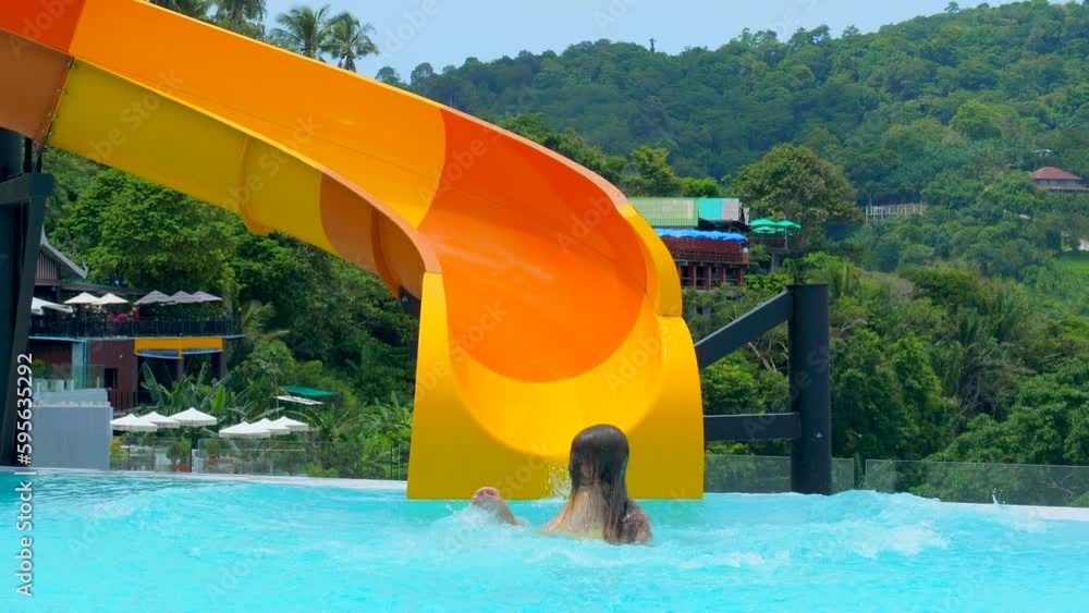 Woman in swimwear slides down a water slide in a swimming pool. Girl ...
