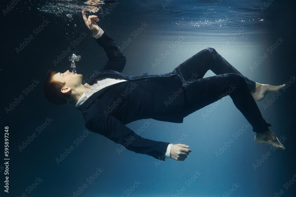 Businessman, a man in a suit, is drowning under water, reaching for the ...