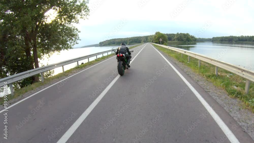 Biker riding on modern sport motorbike through road near lake ...