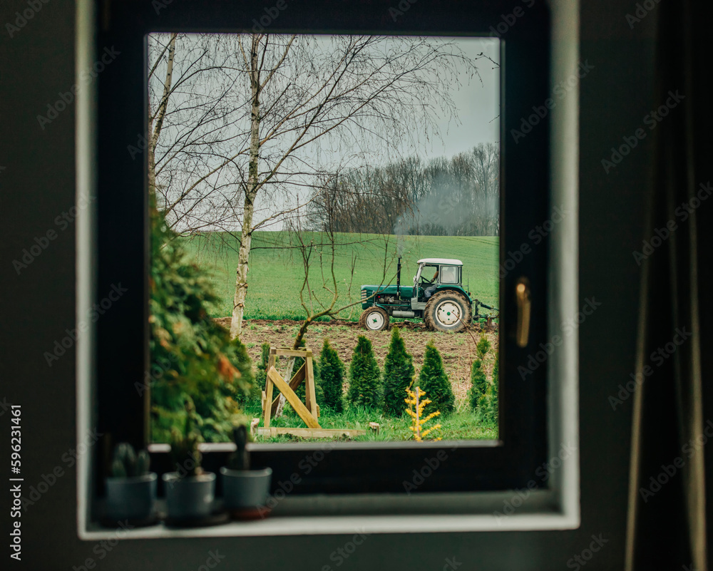 Farmer ploughing with tractor in field seen through window Stock Photo ...
