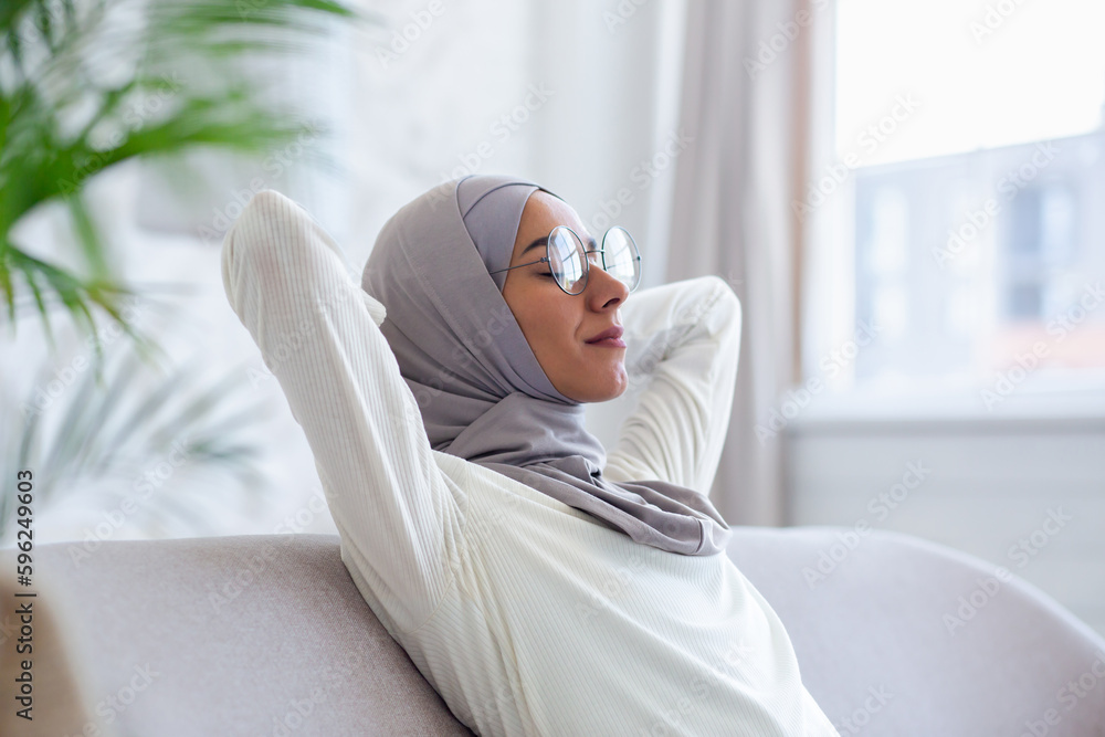 Young muslim woman resting at home with eyes closed hands behind head ...