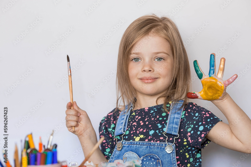 Foto de A happy little girl of 4 years draws. The child's hands are covered with paint. The ...