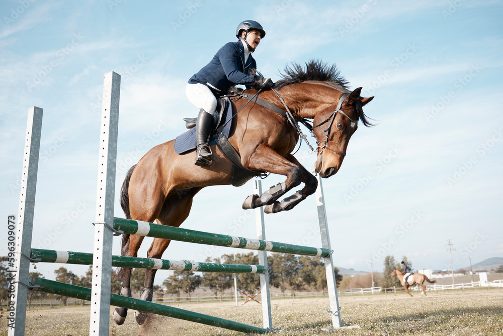Up and over. Full length shot of a young female rider jumping over a ...