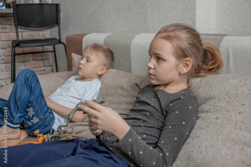 Little brother and sister watch TV together sitting on the sofa in the ...