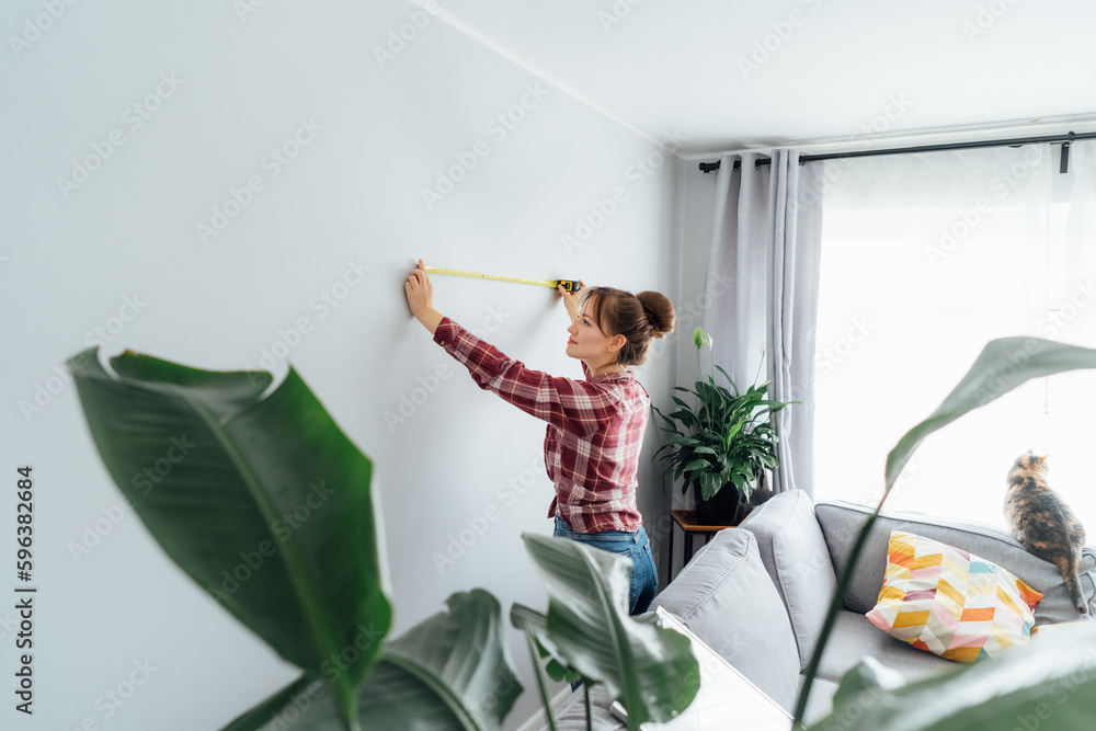 Young woman doing measuring with a measure tape on the wall. Girl wants ...