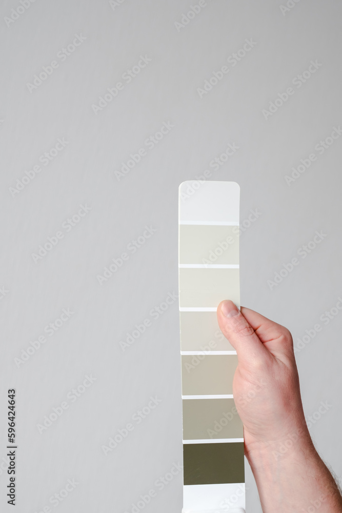 A man's hand holding off white color palette on a gray wall background ...