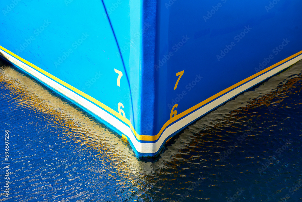 The bow of a large blue ship with yellow and white waterline stripes ...