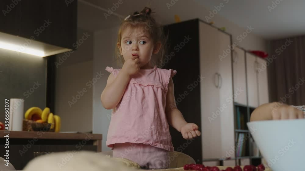 Baby girl standing on the stool at the kitchen table eating the cherry ...
