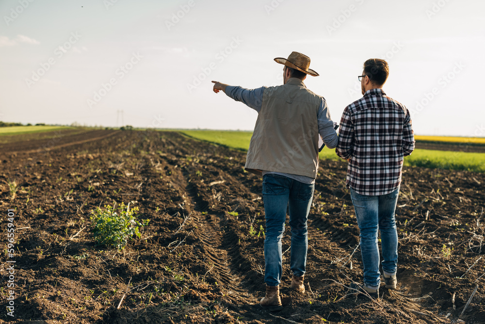 Two farmers are on the field. One man is pointing t the border of the ...