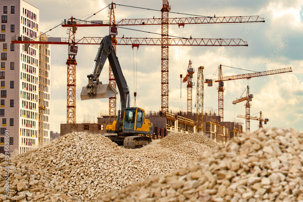 Foto de Multi-storey building. Excavator on mountain of small stones ...