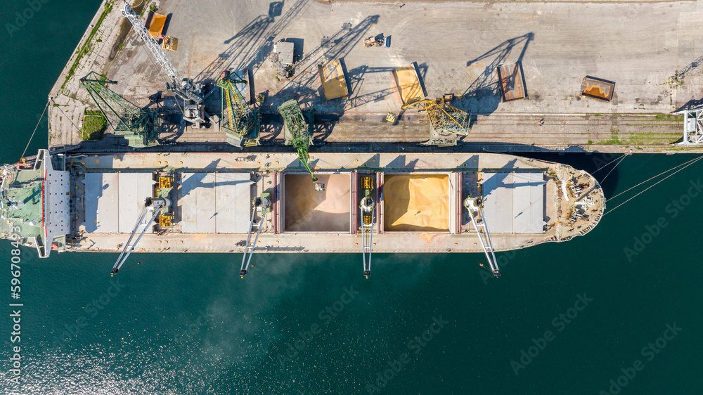 Loading dry cargo ship of wheat by cranes in port. Top down view loading into holds of sea cargo ...