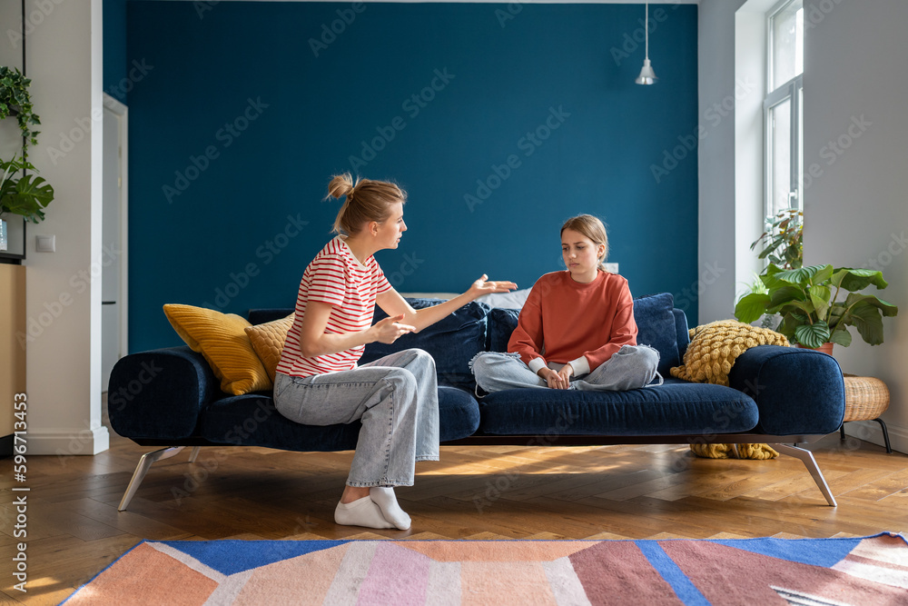 Foto de Upset teen girl sitting on sofa listening angry mother scolding her for bad school ...