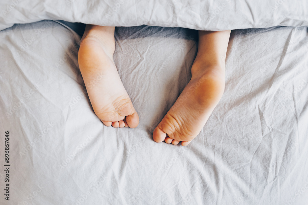 Kids child legs feet lying on pillows in bed at home. Child playing ...