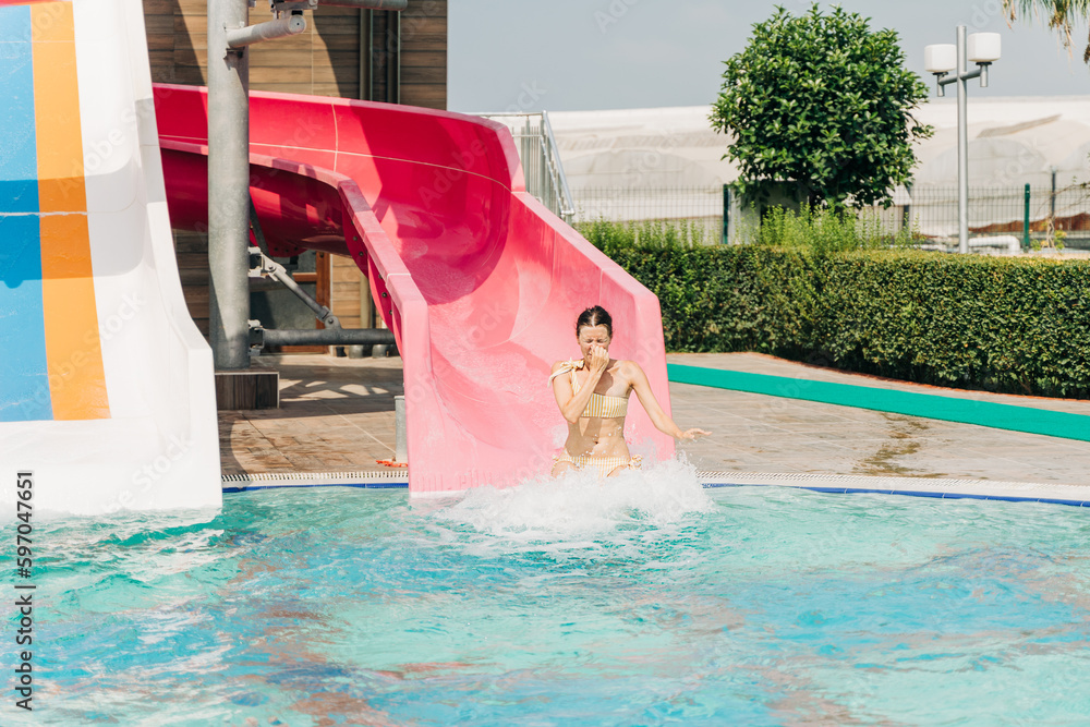 Young woman slide in pool after going down water slide at sunny day in ...