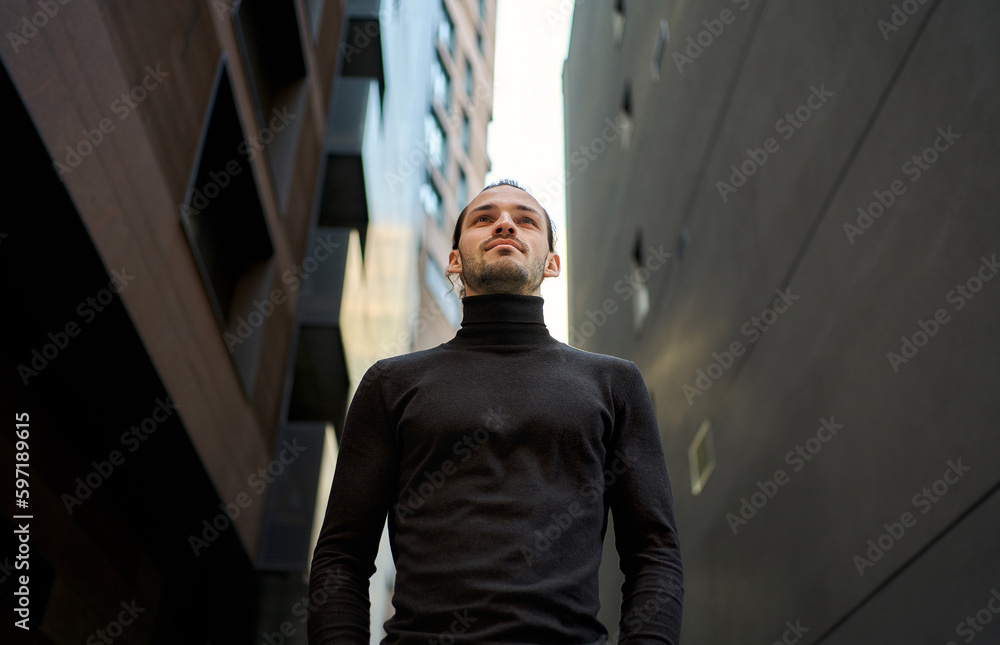 Poster Confident ambitious man standing between two tall buildings with skyline, looking ahead ...