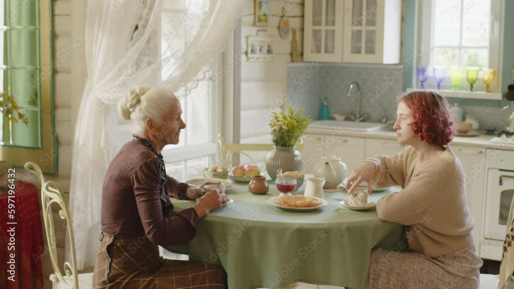 Side view shot of young gen Z girl and her grandmother sitting at table ...
