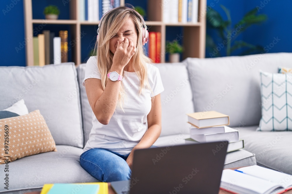 Young blonde woman studying using computer laptop at home smelling ...