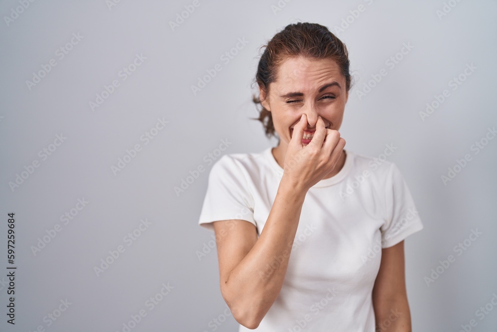 Beautiful brunette woman standing over isolated background smelling ...