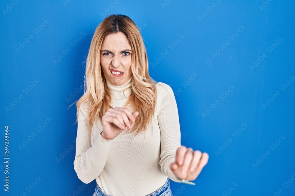 Young caucasian woman standing over blue background disgusted ...